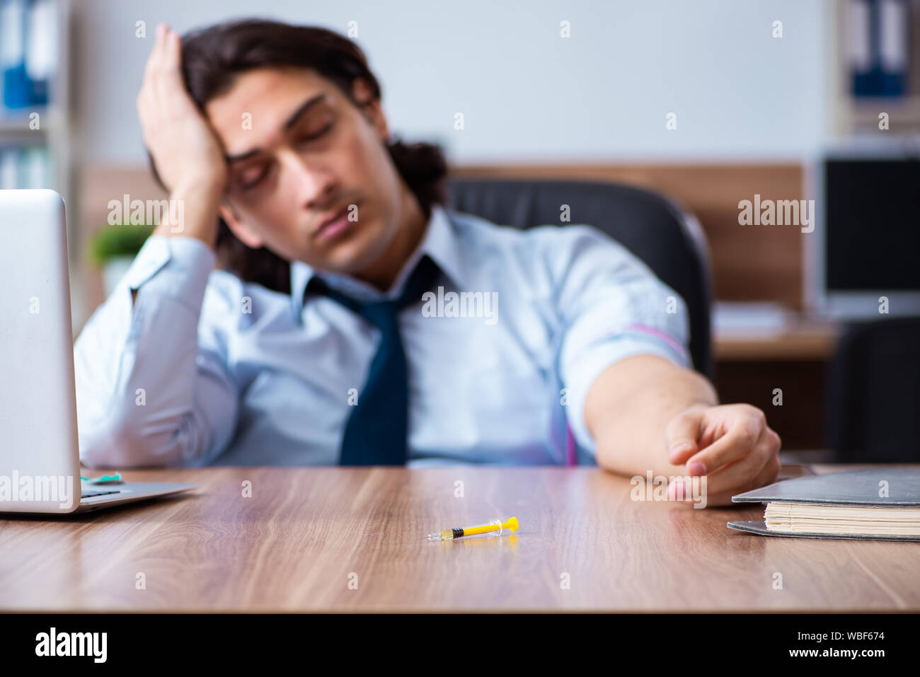 The young man having problems with narcotics at workplace Stock Photo ...