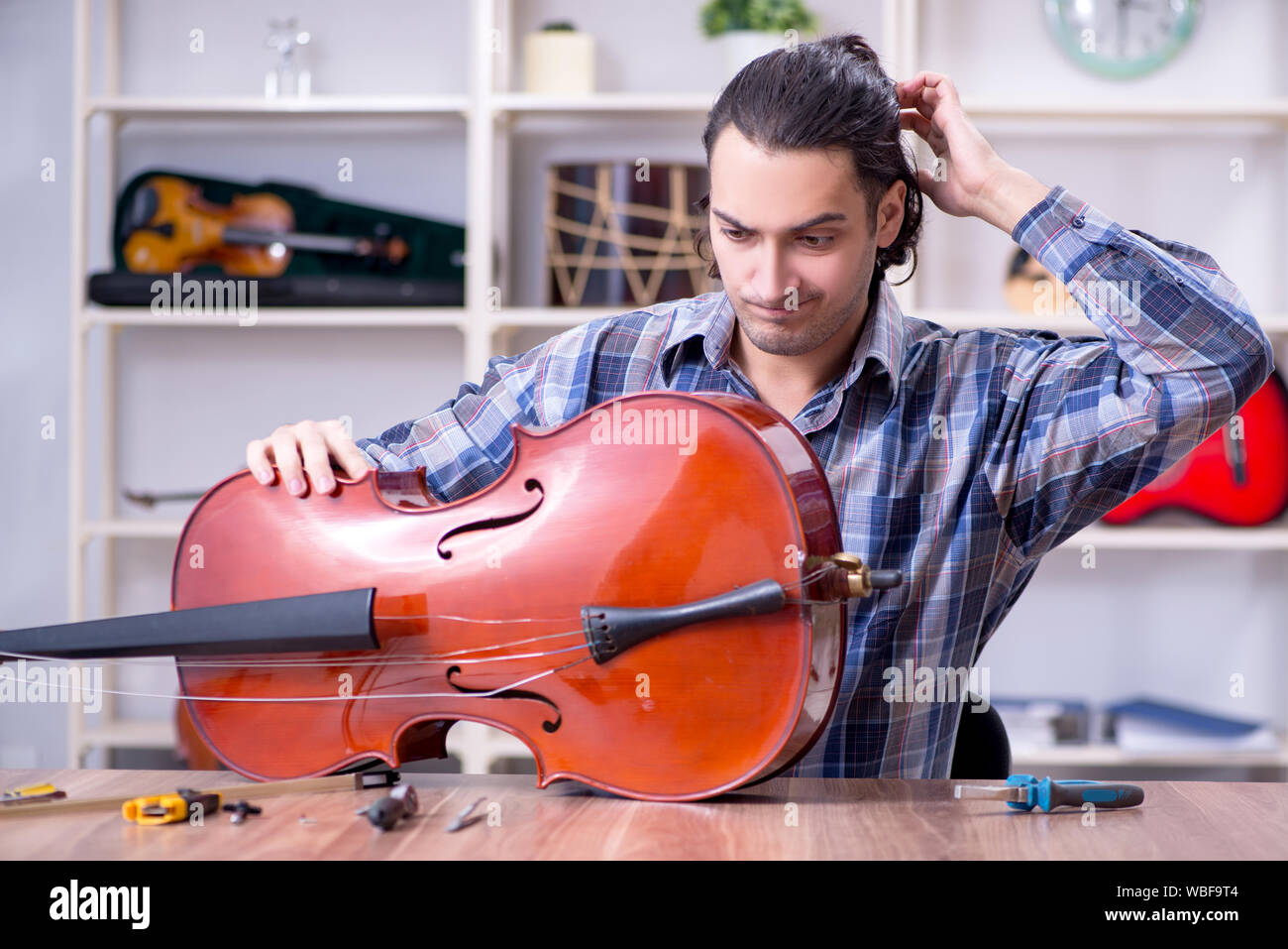 The young handsome repairman repairing cello Stock Photo - Alamy