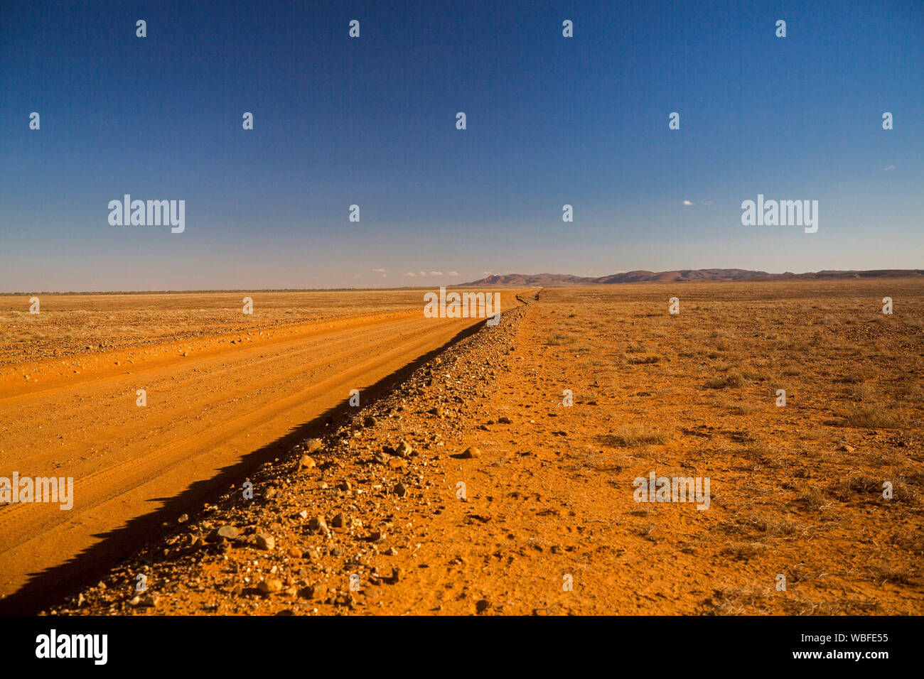 Outback landscape with dirt track stretching across barren red plains ...
