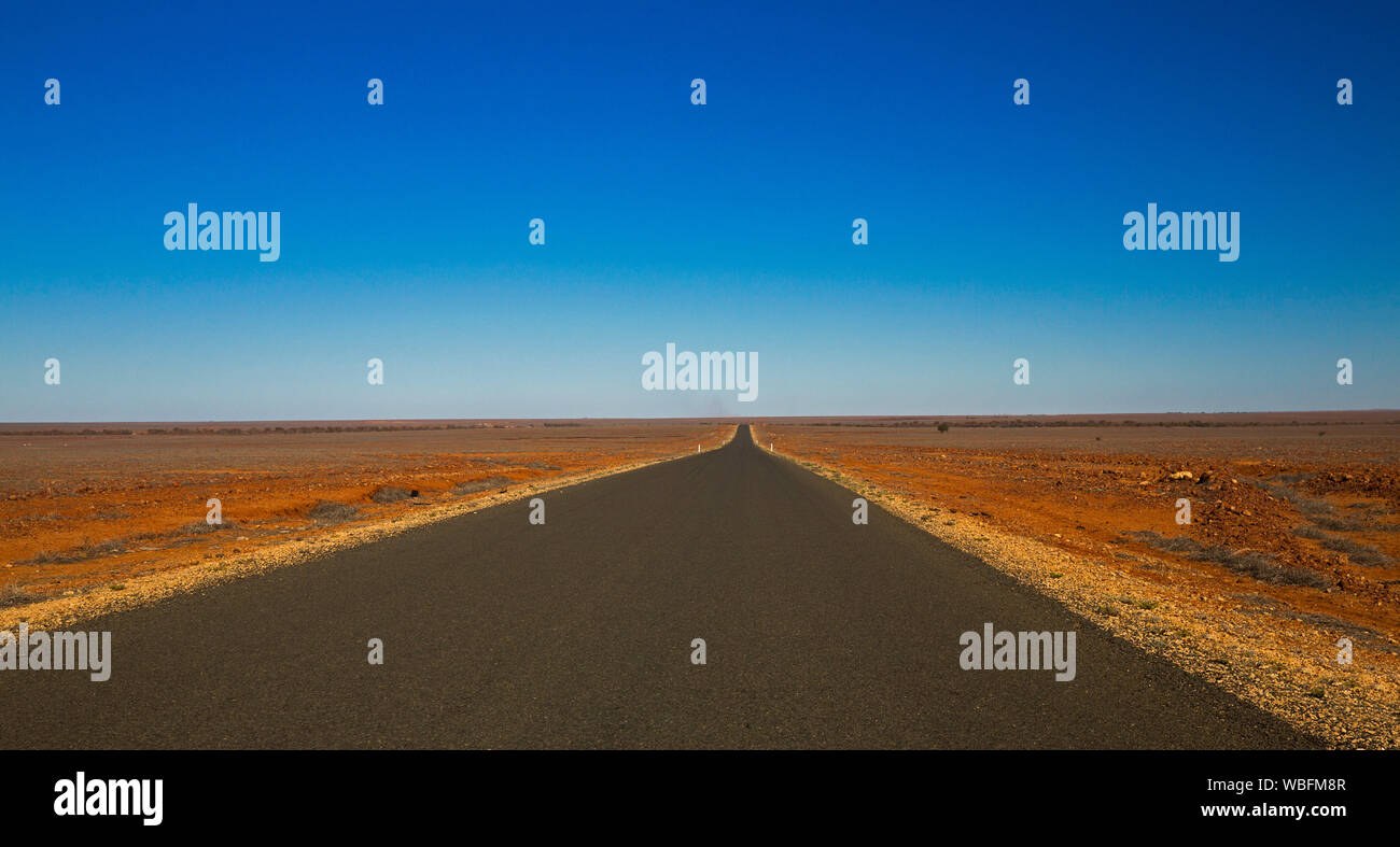 Long straight bitumen road stretching across barren red Australian ...