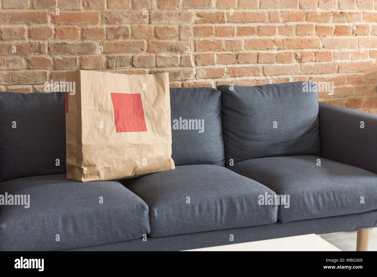 Blank paper gift or shopping bag standing on blue modern sofa. Empty ...