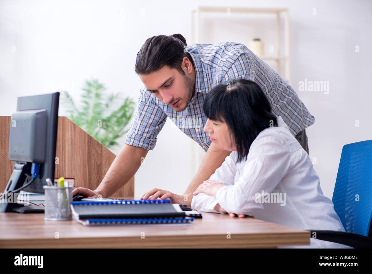 Young male employee explaining to old female colleague how to use ...