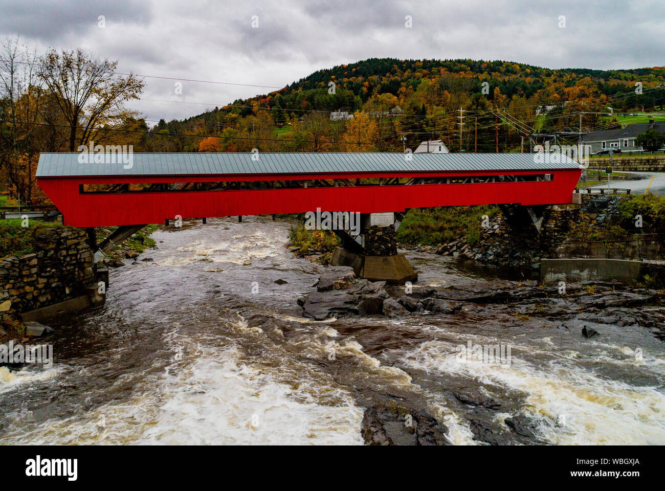 A red covered bridge first built in 1883 spans a rapidly flowing river ...