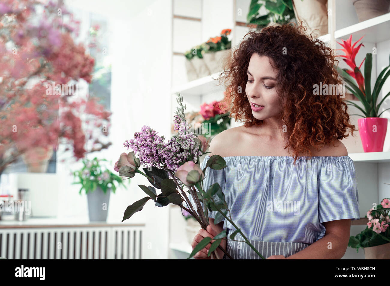 Focused young redhead woman mixing flowers while composing bouquet ...