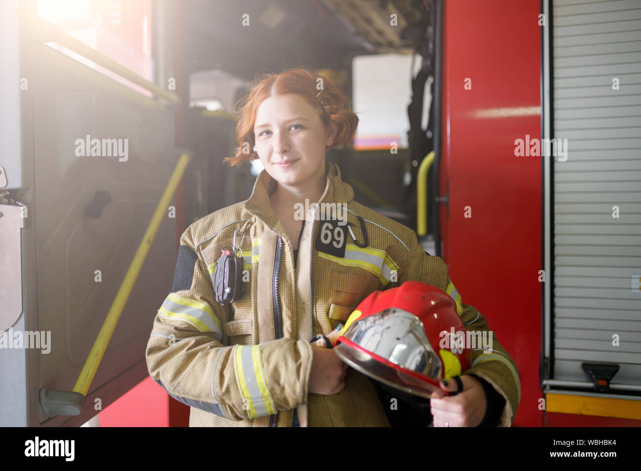 Photo of ginger woman firefighter with helmet in hands against backdrop ...