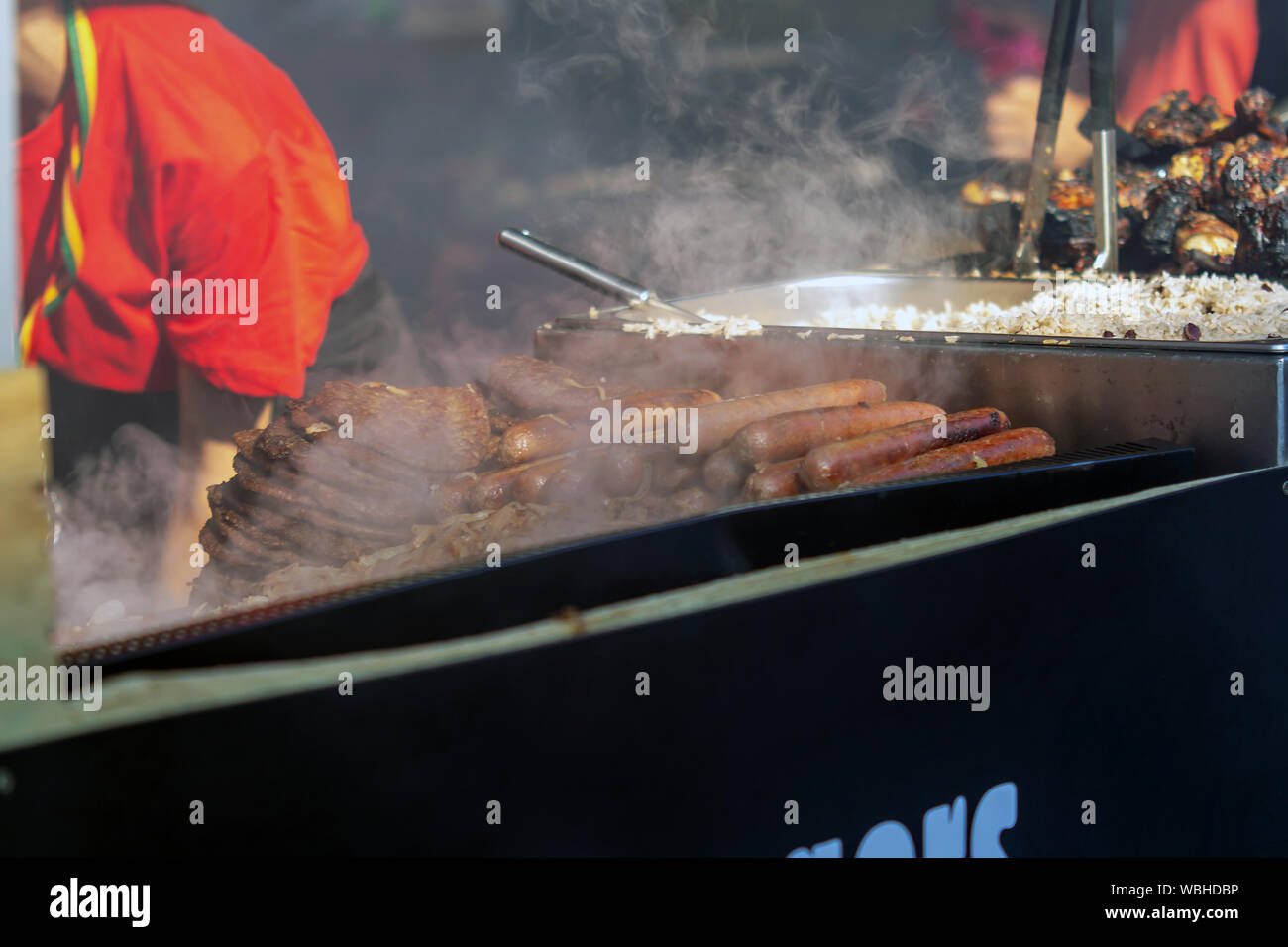 Food is cooked over a barbeque, including burgers, sausages, jerk ...