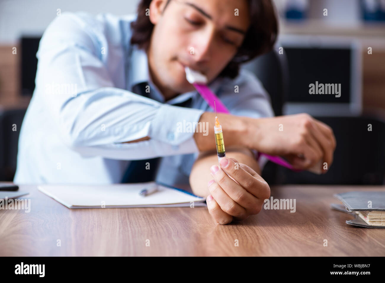 The young man having problems with narcotics at workplace Stock Photo ...