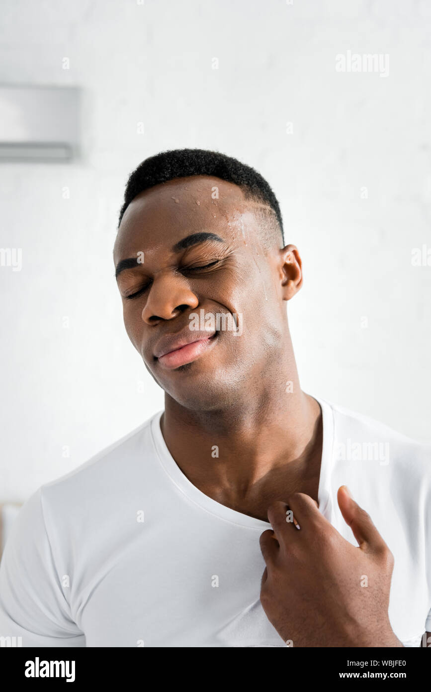 exhausted african american man closing eyes and standing in room with ...