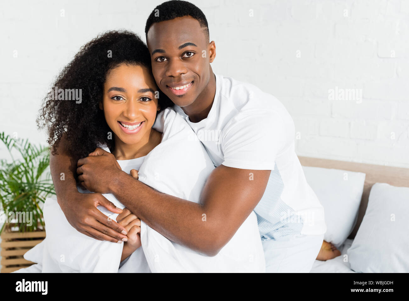 african american couple cuddling to each other and looking at camera ...