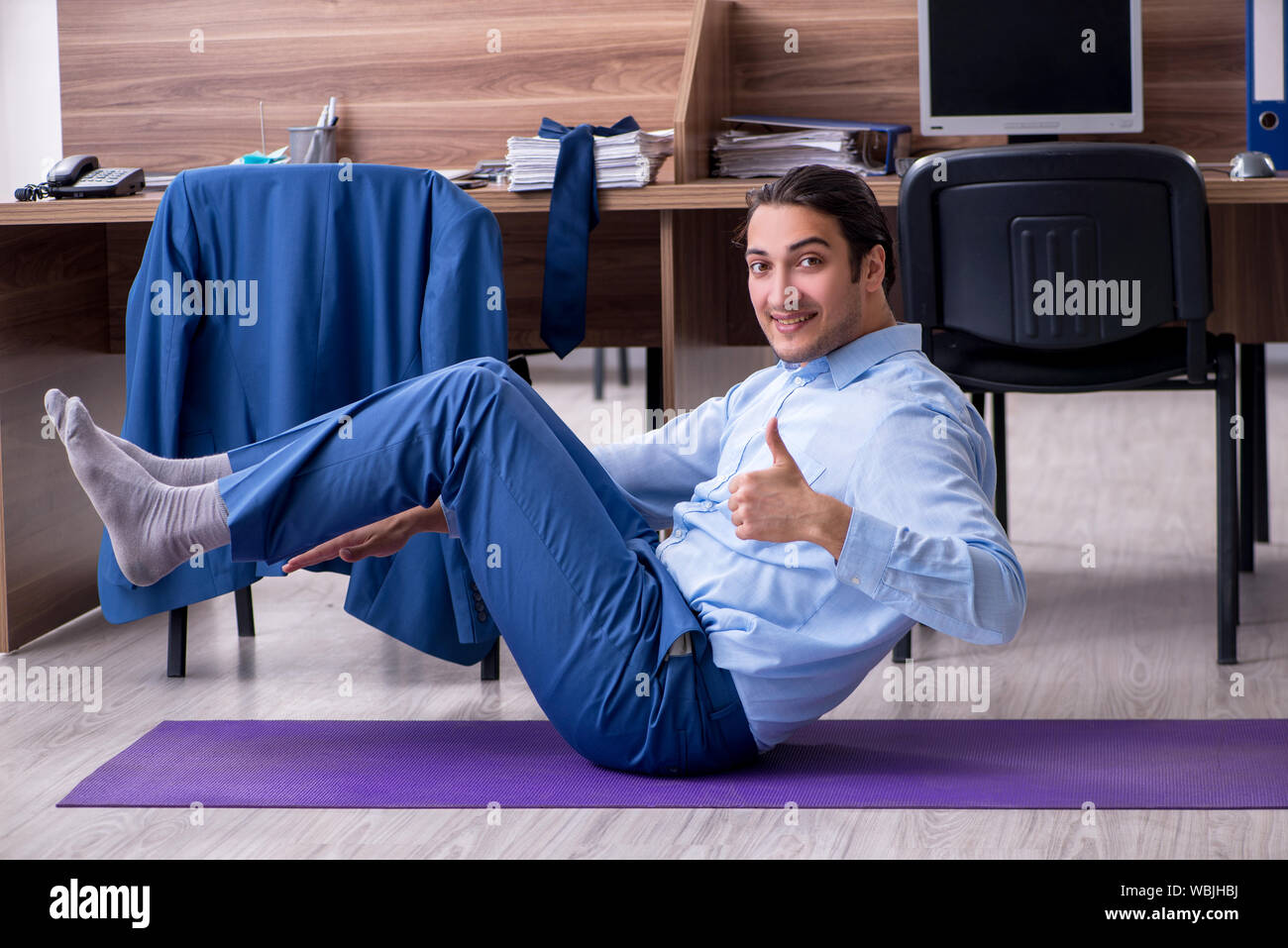 The young handsome businessman doing exercises at workplace Stock Photo ...
