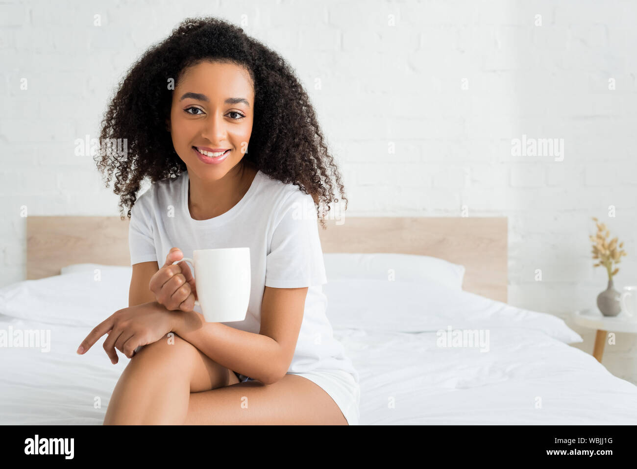 happy african american woman sitting with cup on bed in room Stock ...