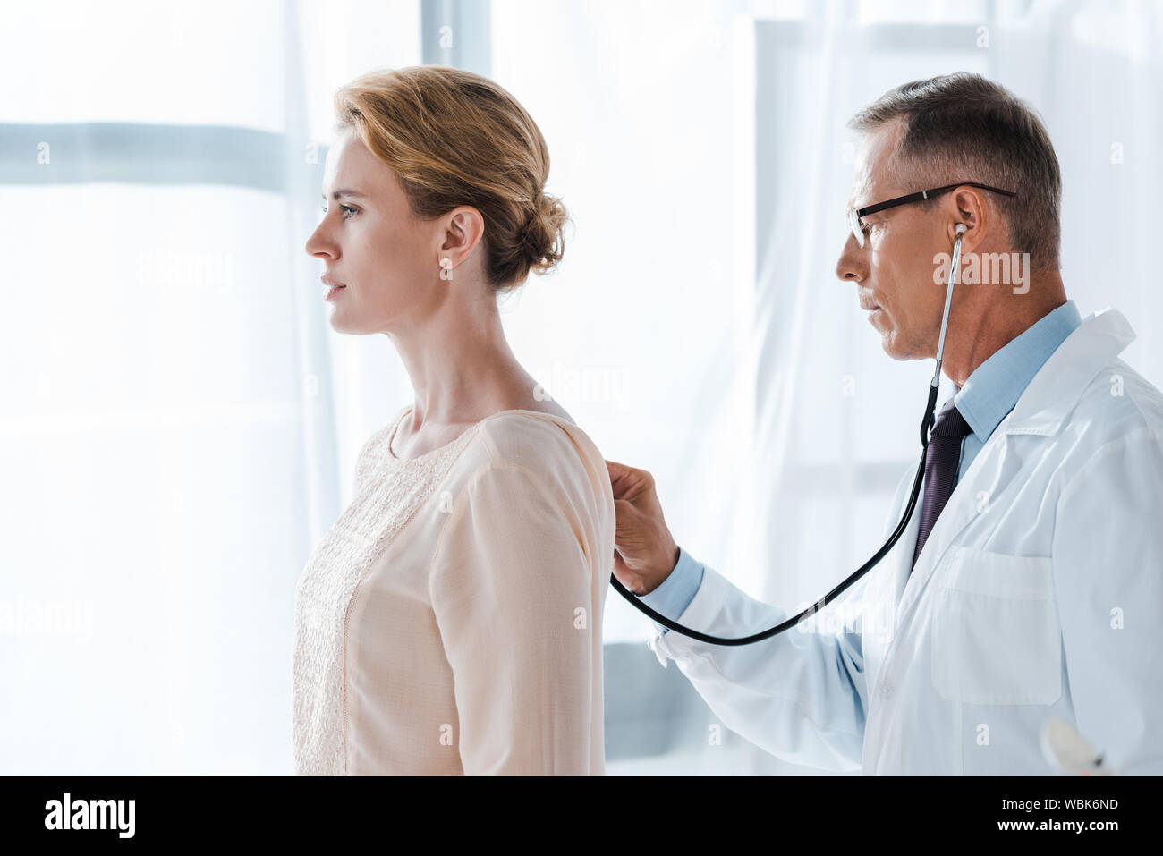 side view of doctor in glasses using stethoscope while examining ...