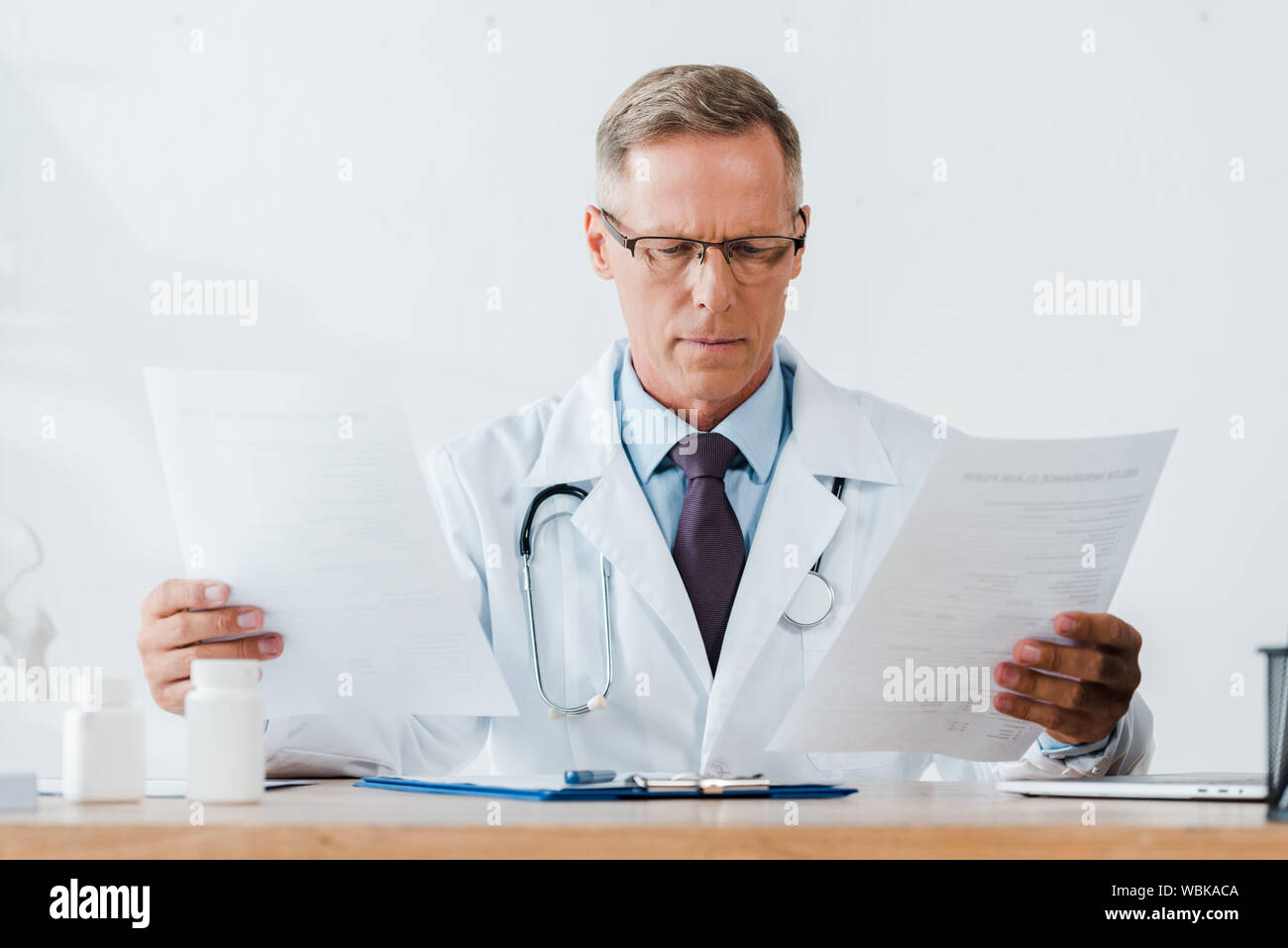 doctor in glasses and white coat with stethoscope looking at documents ...