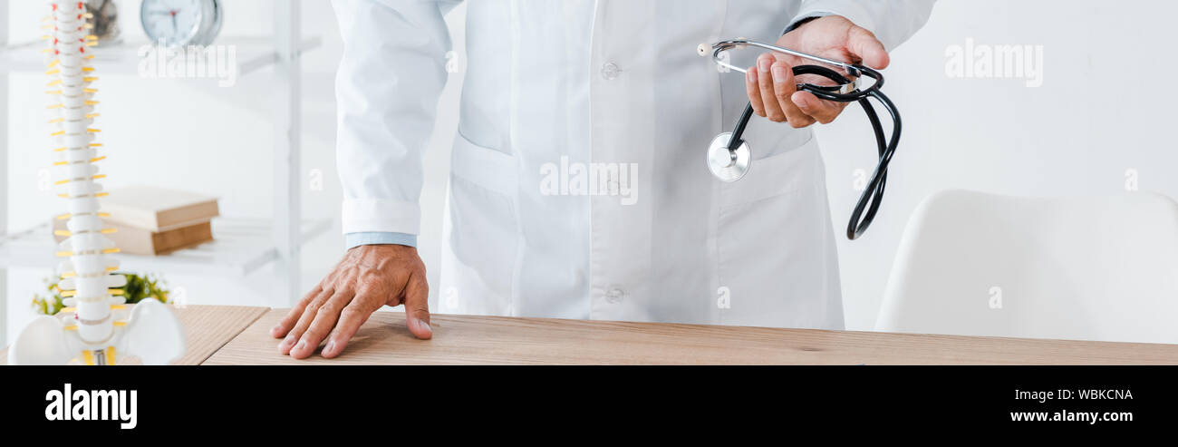 panoramic shot of doctor holding stethoscope near table in clinic Stock ...
