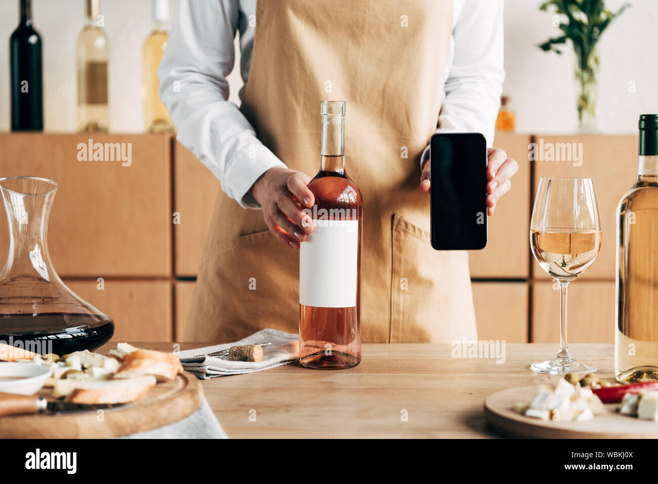 partial view of sommelier in apron standing near table with bottles of ...