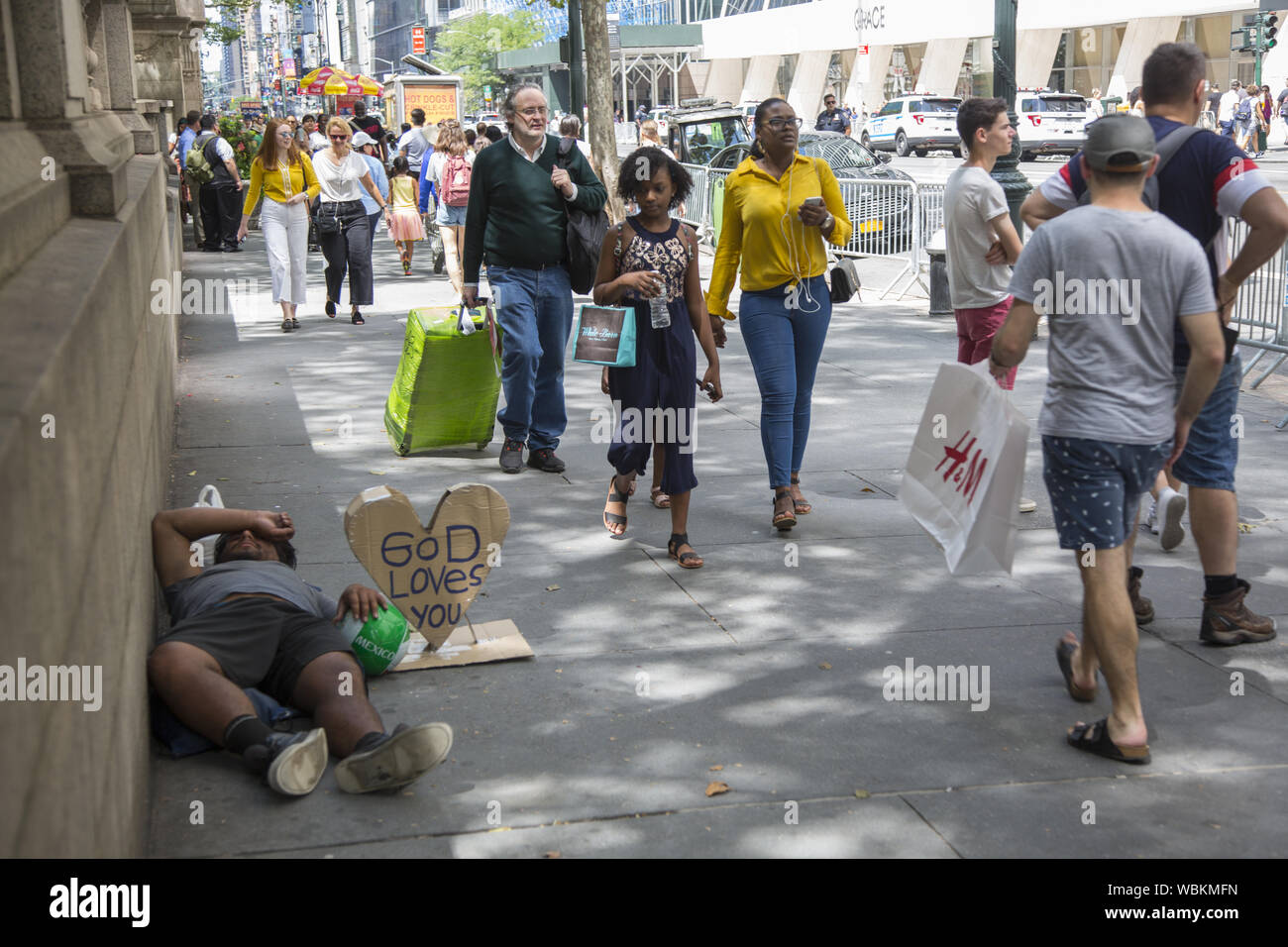 Homeless man with a sign, "God Loves You" rests on the sidewalk, while ...