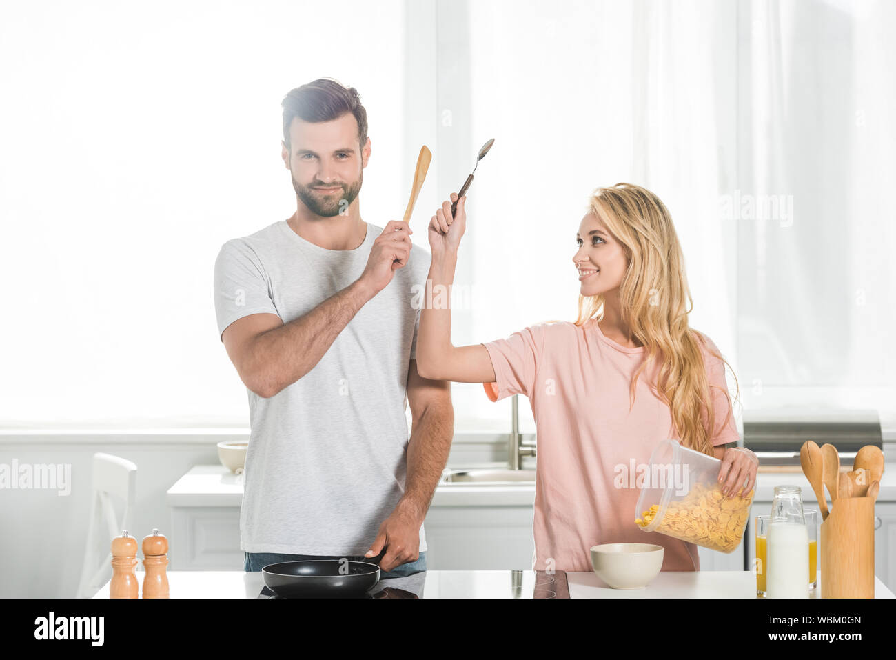 beautiful couple holding spatula and spoon while cooking breakfast ...
