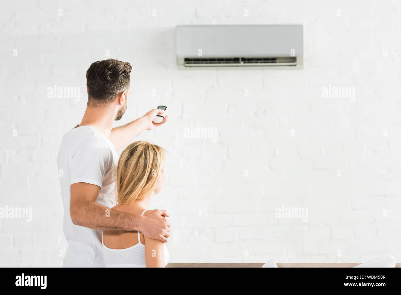 back view of couple with remote control suffering from heat under air ...
