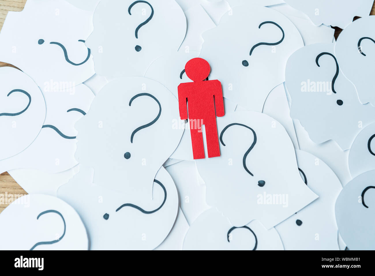 red human shape near question marks on paper with human heads on wooden ...