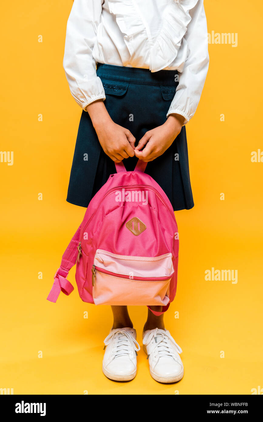 cropped view of schoolkid holding backpack and standing on orange Stock ...