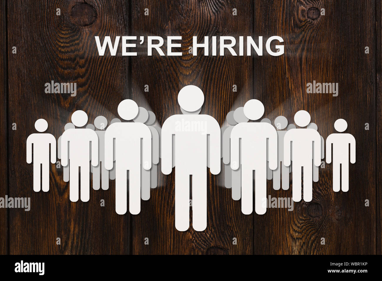 Paper men on wooden background with text WE'RE HIRING. Business concept ...