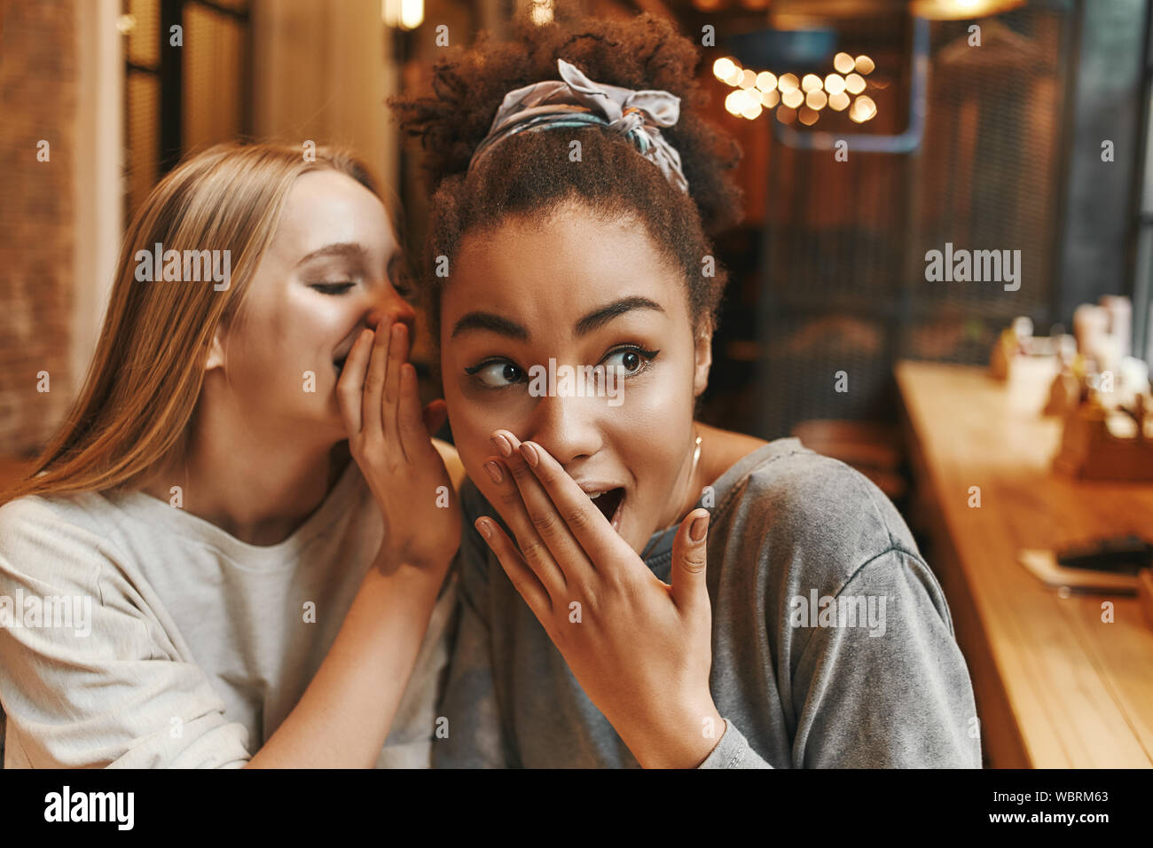 Close up portrait of two multiracial young colleagues gossiping while ...