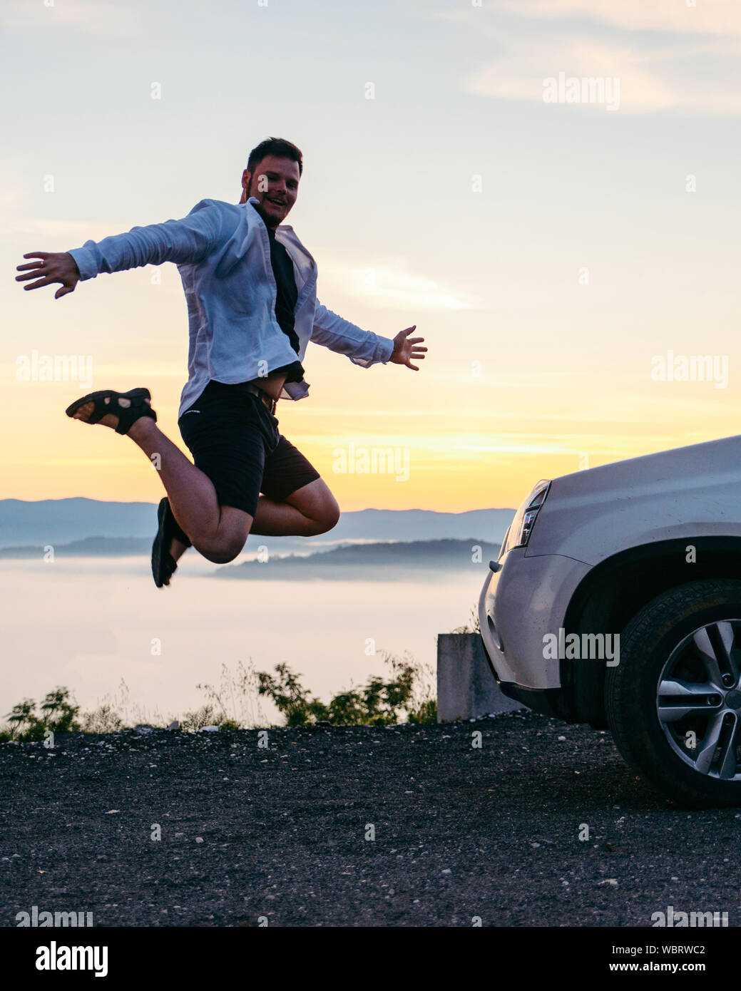 man jumping near white suv car sunrise above mountains foggy weather ...