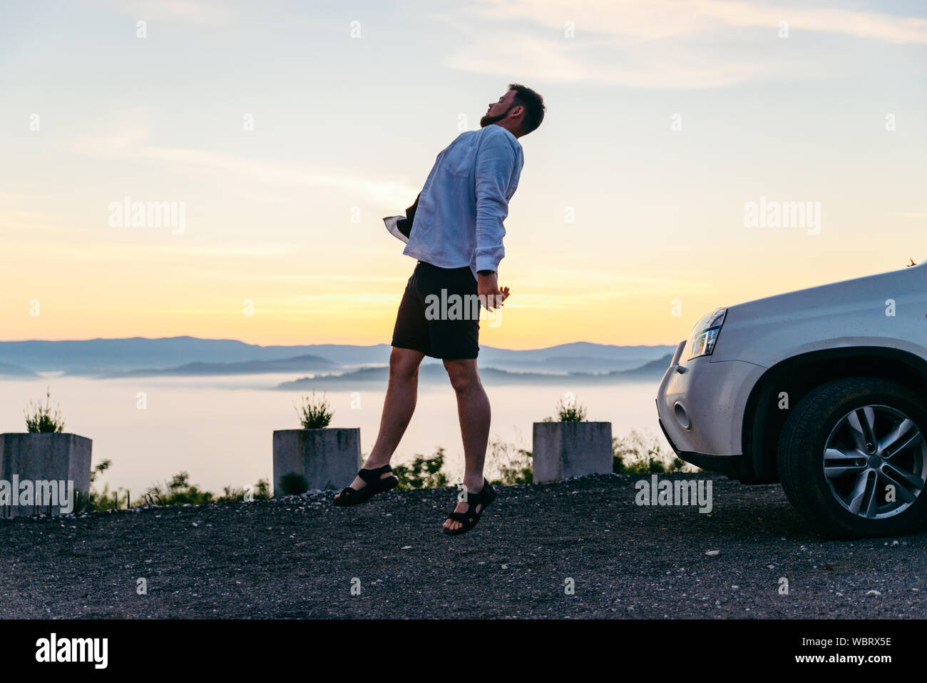 man jumping near white suv car sunrise above mountains foggy weather ...