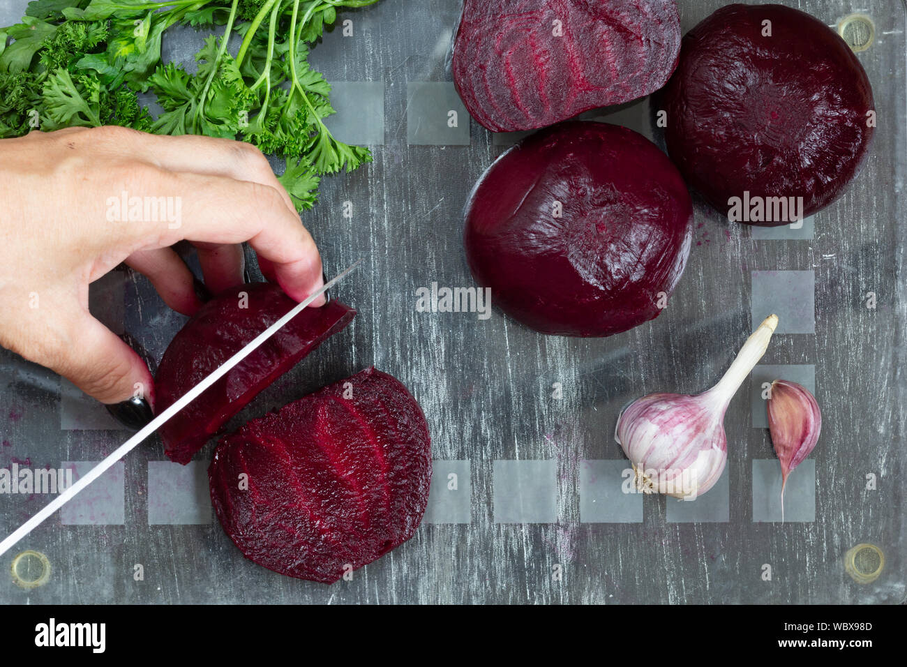 Woman hand cutting roots of cooked peeled beet on black background ...