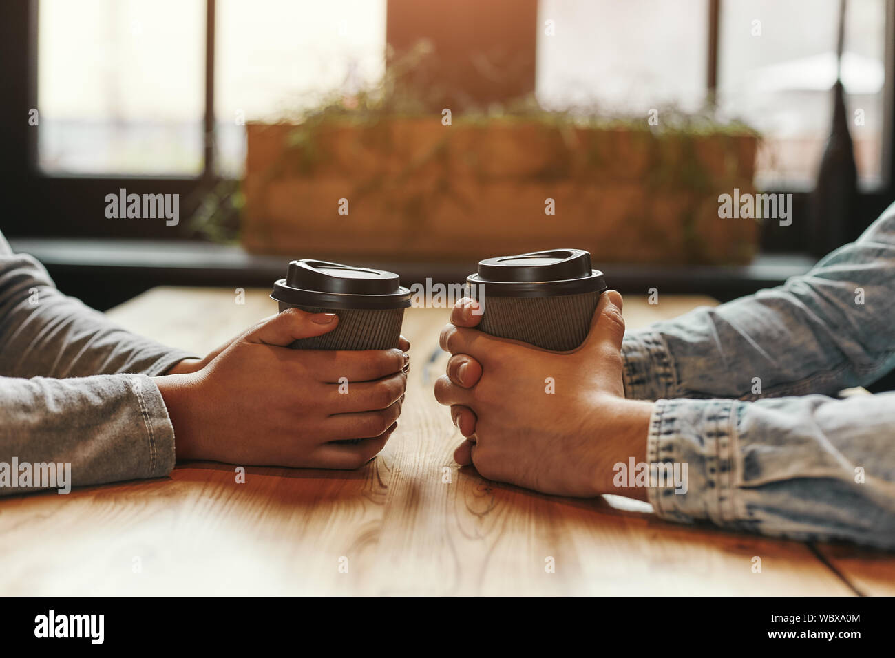 Close up shot of hands of two young colleagues sitting in a cafeteria ...