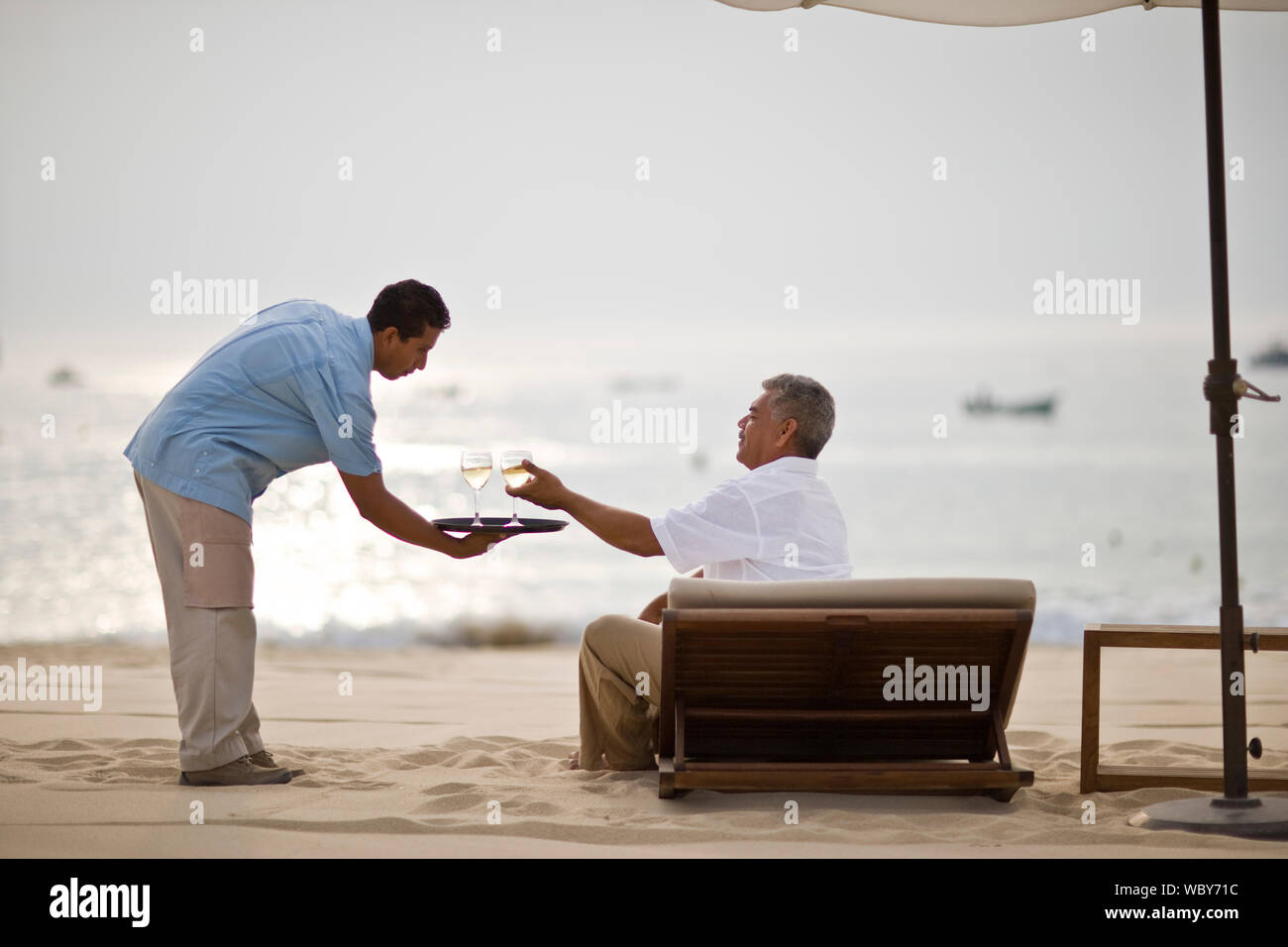 Beach resort waiter serving wine to man on sun lounger Stock Photo - Alamy
