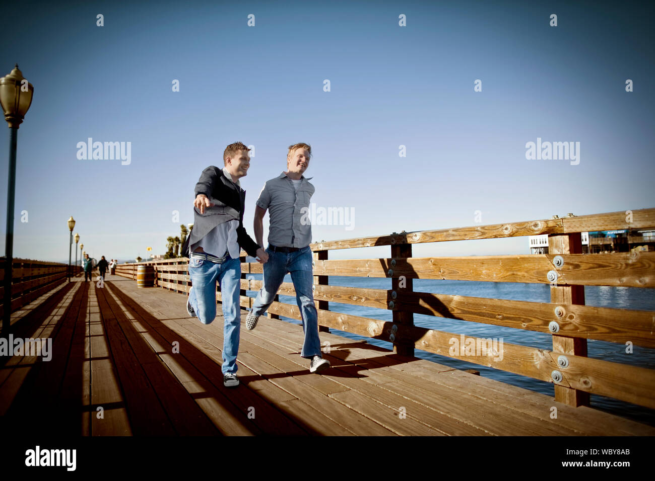 Gay couple running along pier together Stock Photo - Alamy