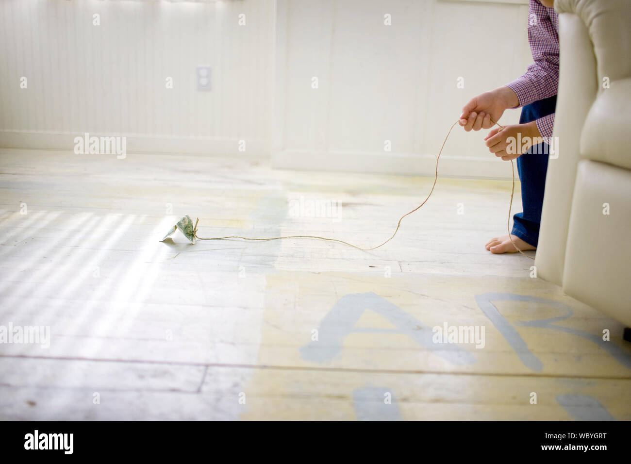 Child hiding behind a chair holding onto string with paper money ...