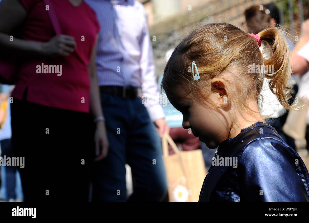 Pensive little girl walking. Parents in the background. Family negative ...