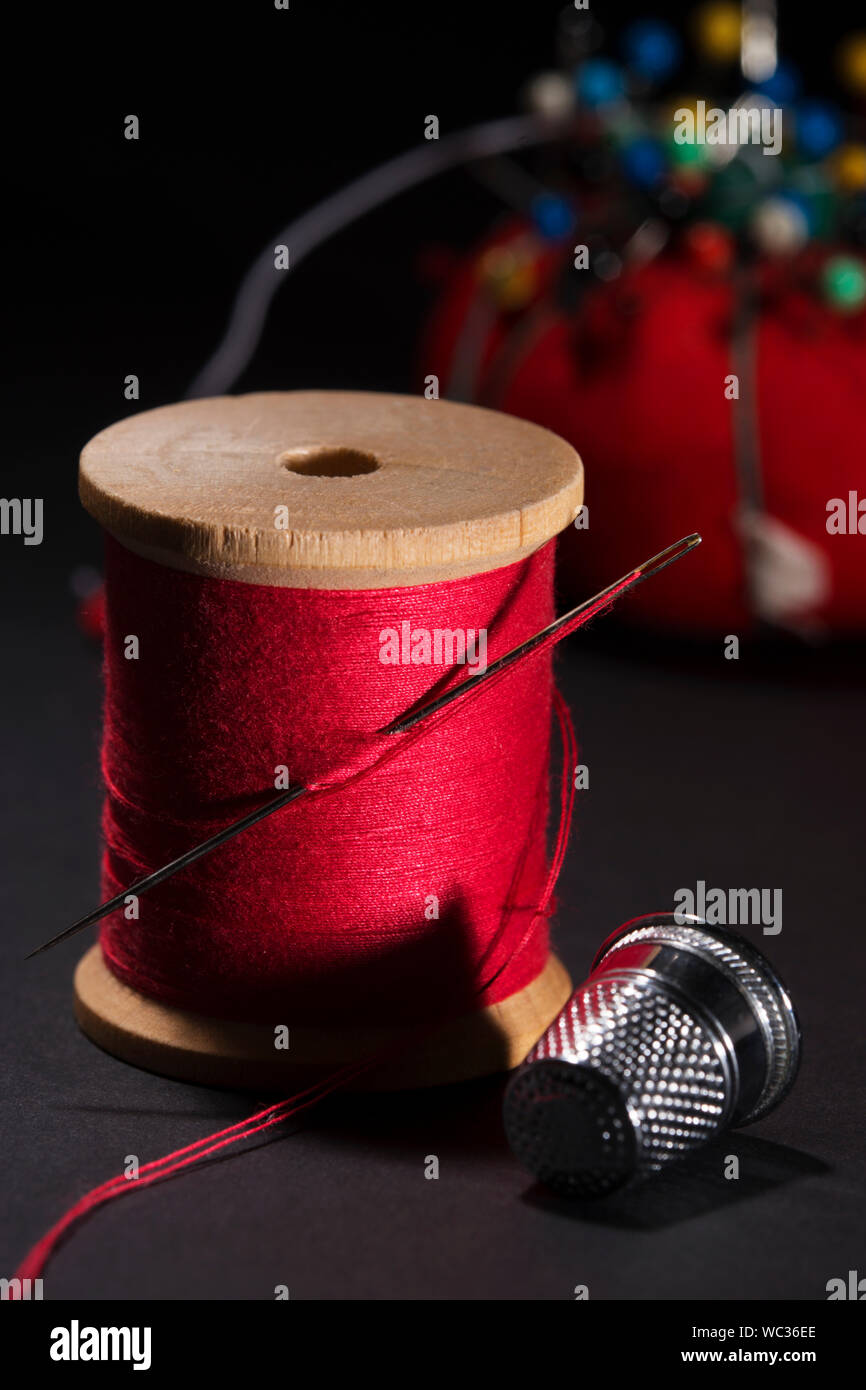 Close up of sewing tools. Wooden spool of red thread with threaded ...