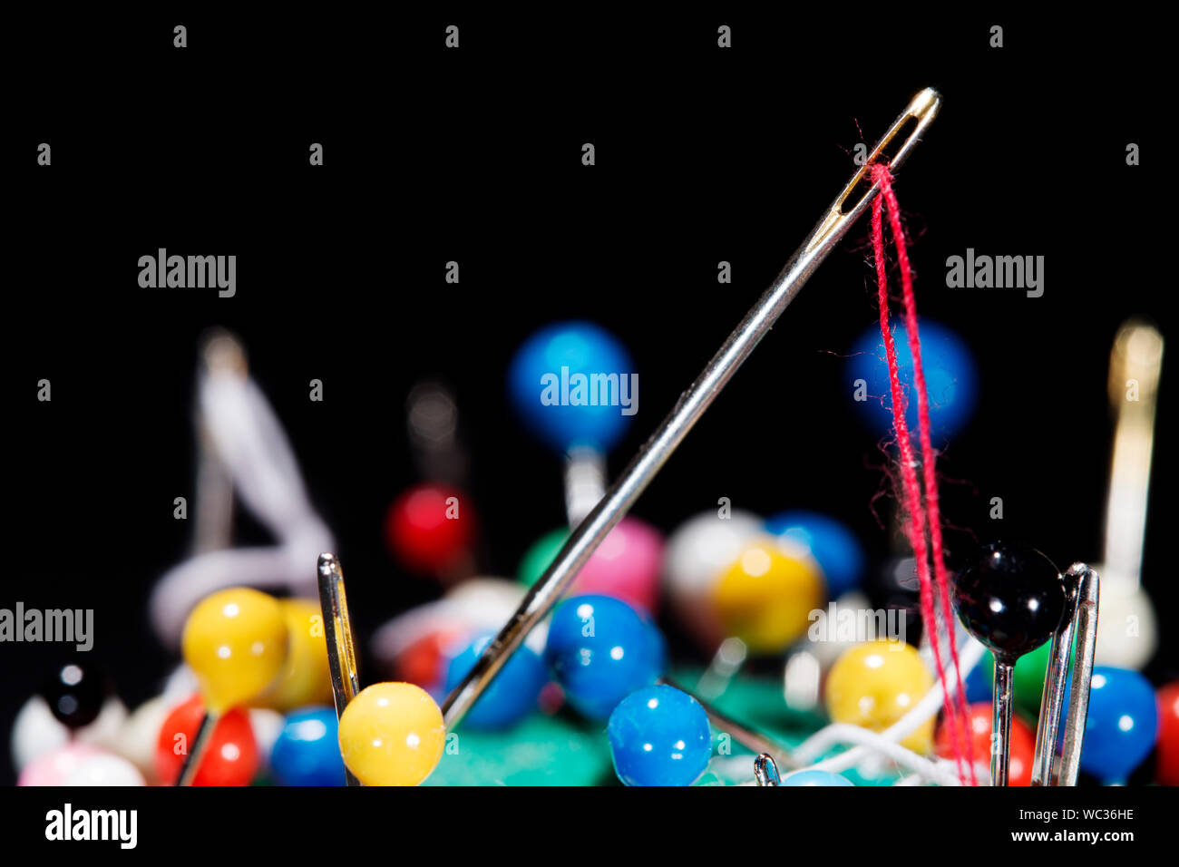 Close up of sewing tools. Needle and red thread stuck in pin cushion ...