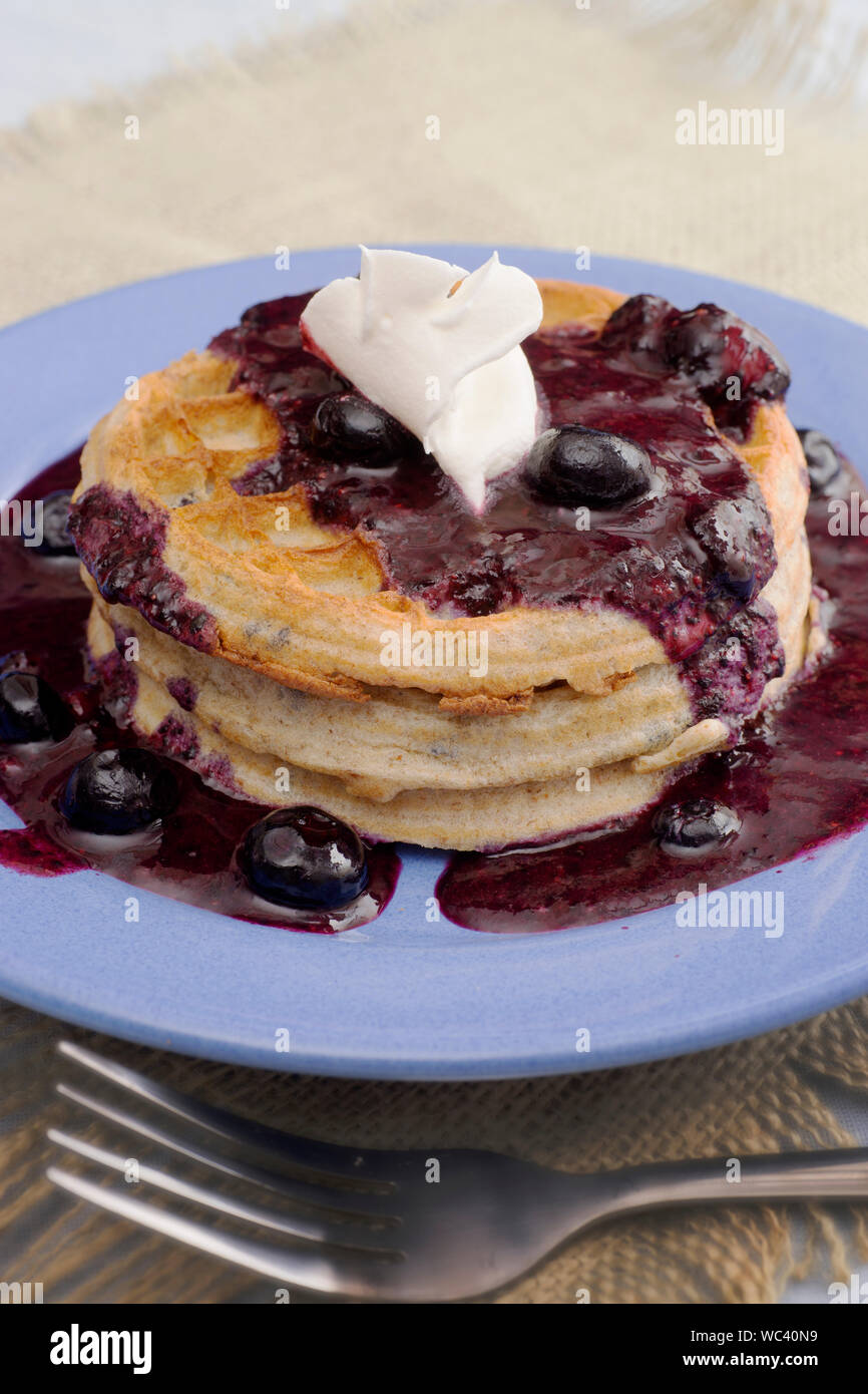 Stack of three blueberry waffles with whipped cream and syrup-on blue ...