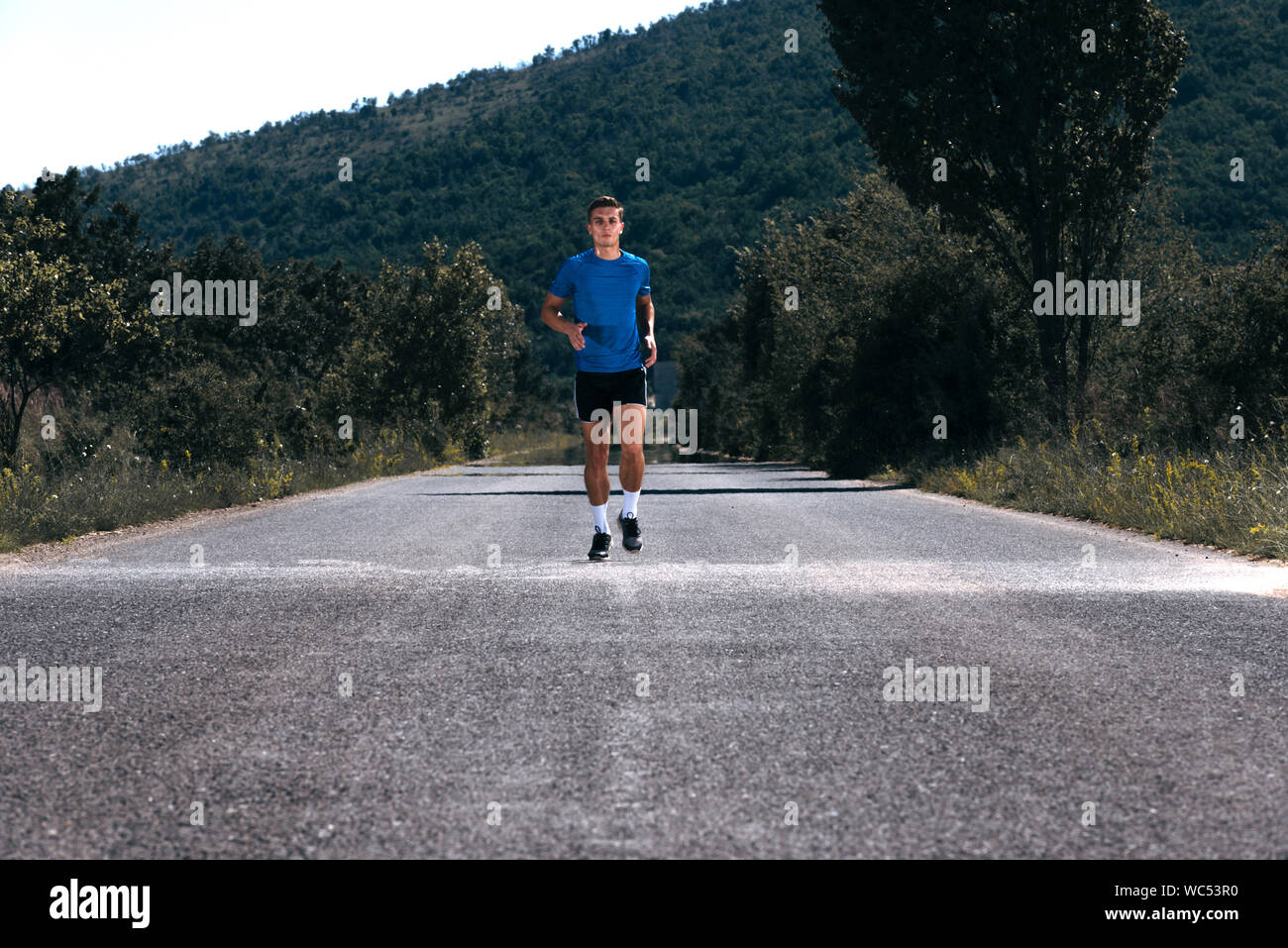 Male athlete running on an empty road in the woods while trying to get ...
