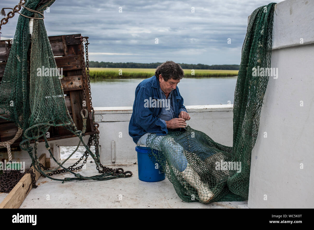 Commercial fisherman mends his net on the deck of a boat Stock Photo ...