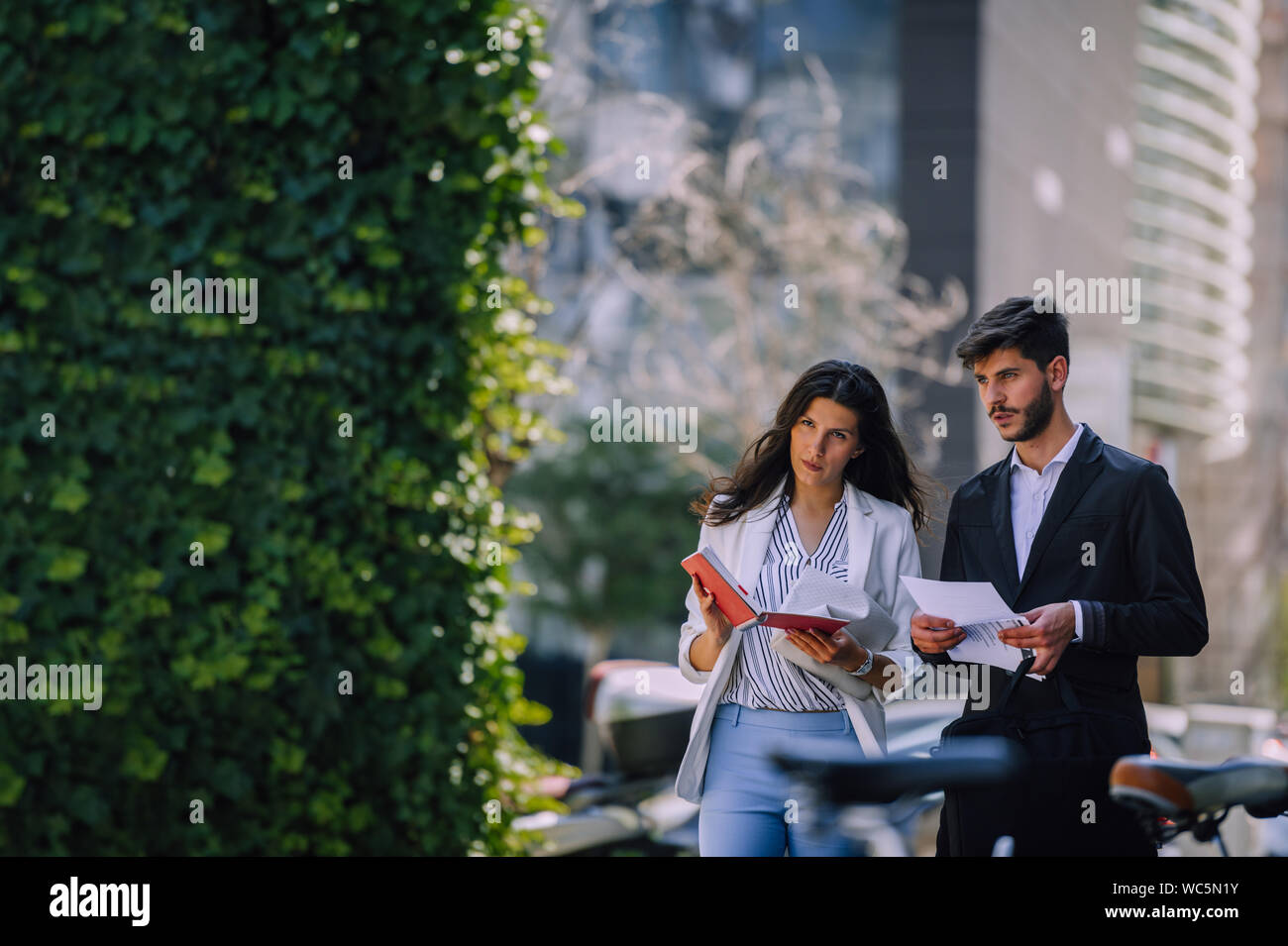 Two business people standing at outside company and looking on papers ...