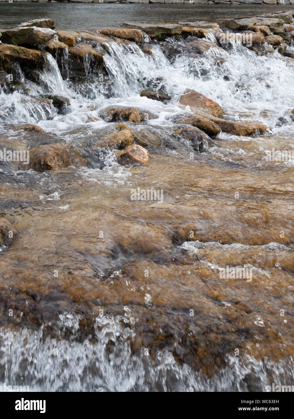 Water cascading over brown and rust-colored rocks with the river in the ...