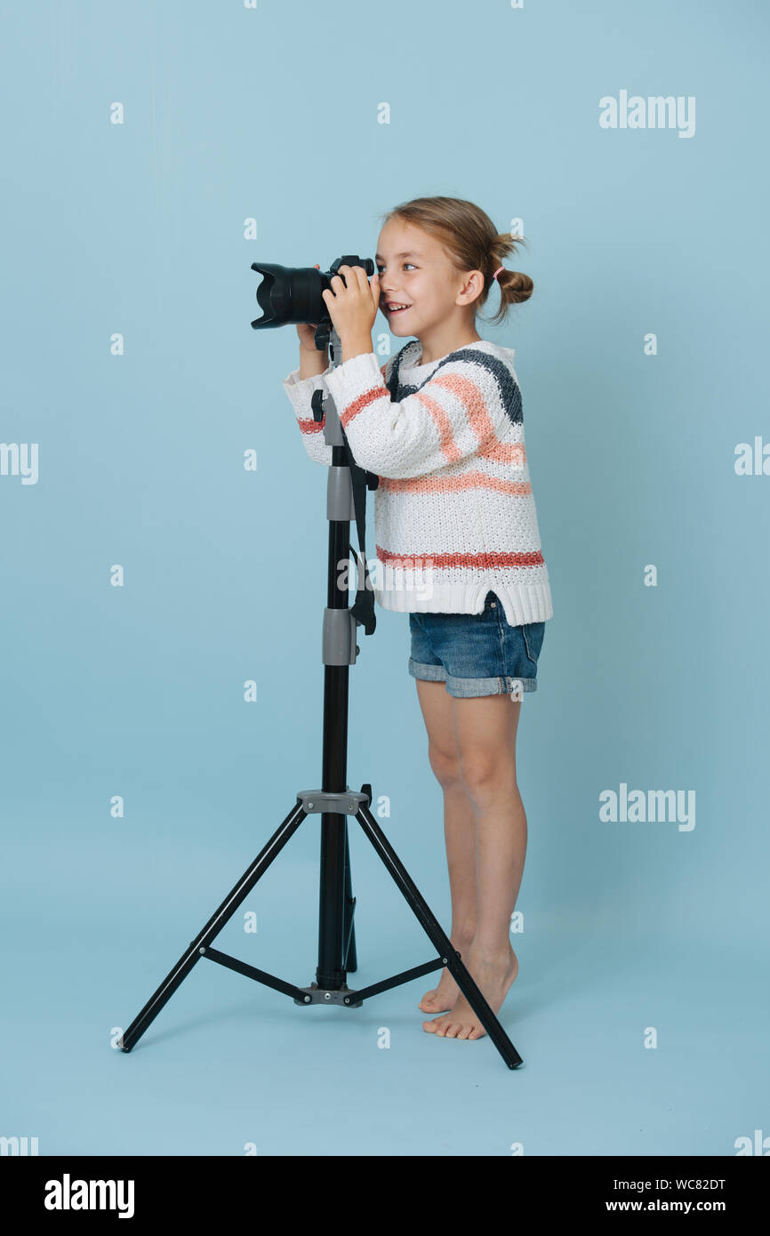Little girl standing on her toes looking in the camera on tripod ...