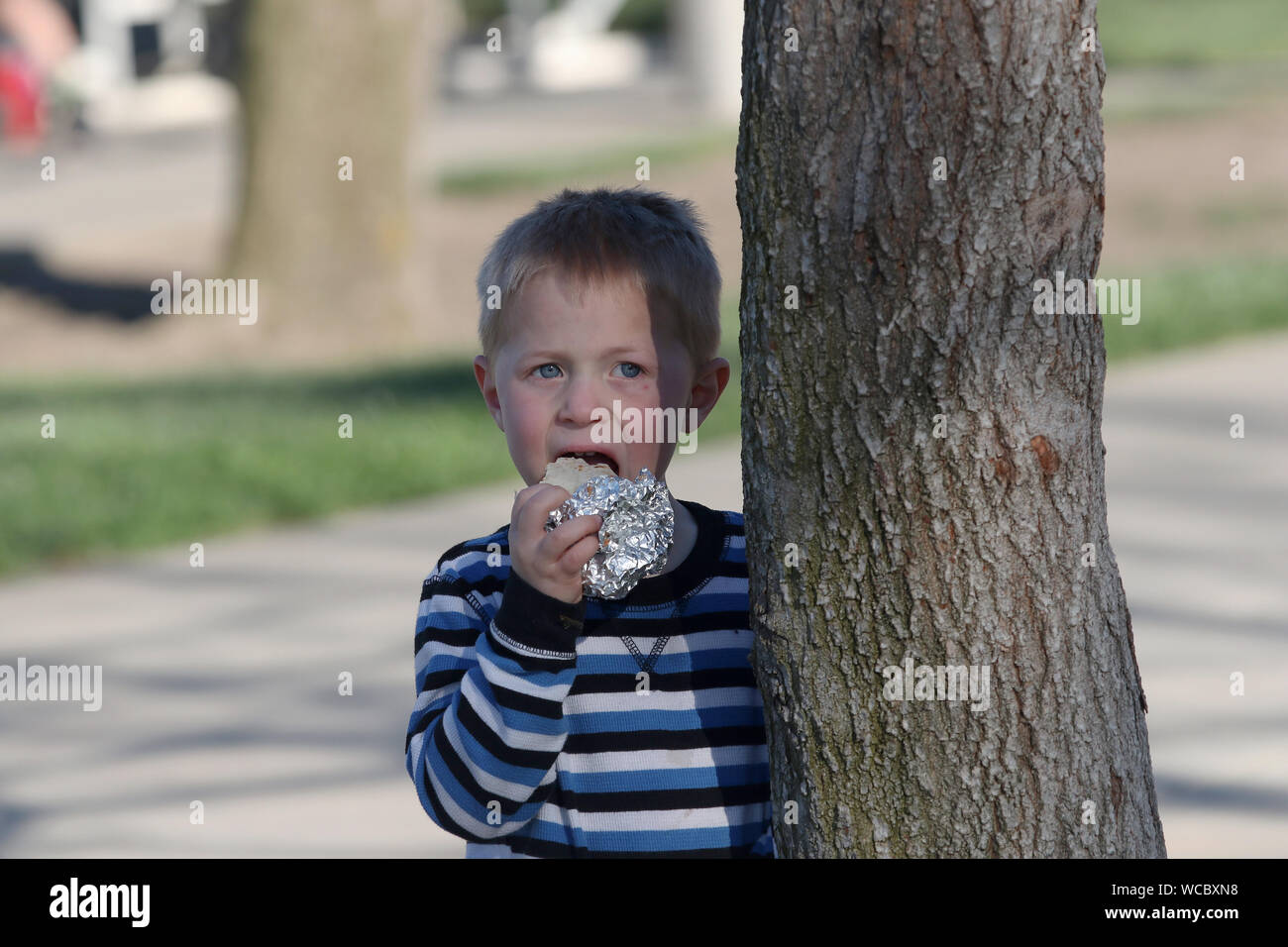 Young boy sneaking a burrito from the table hiding Stock Photo - Alamy