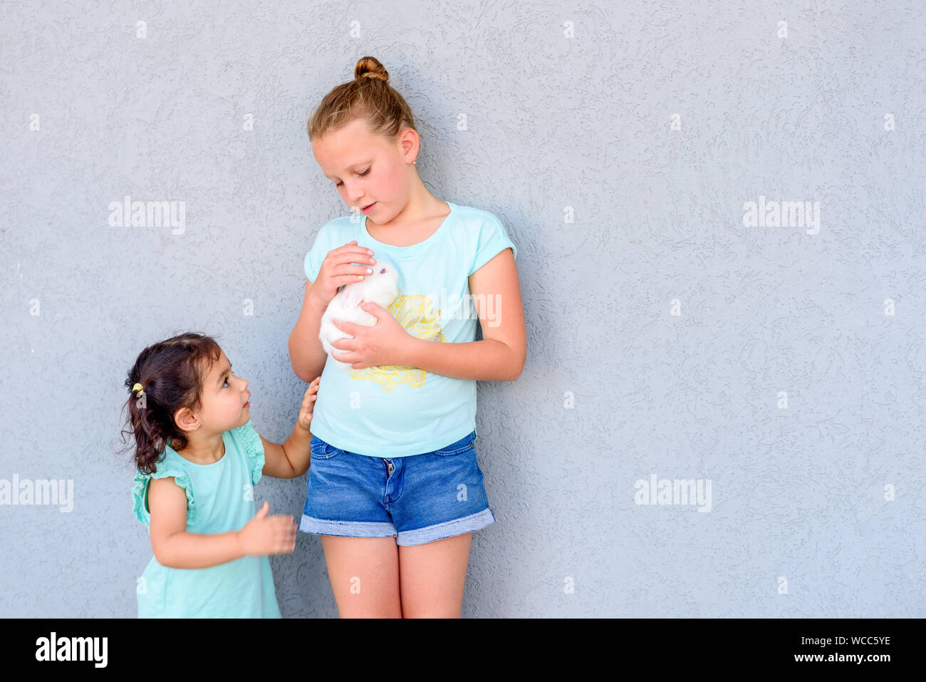 Teenager child holding a cute little white rabbit.Two happy young girls ...