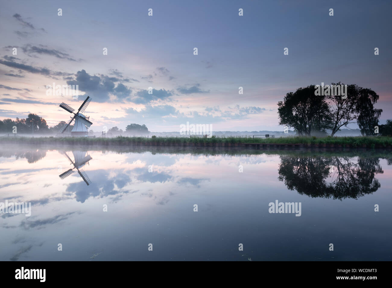 white windmill by river with sky reflection at dawn Stock Photo - Alamy