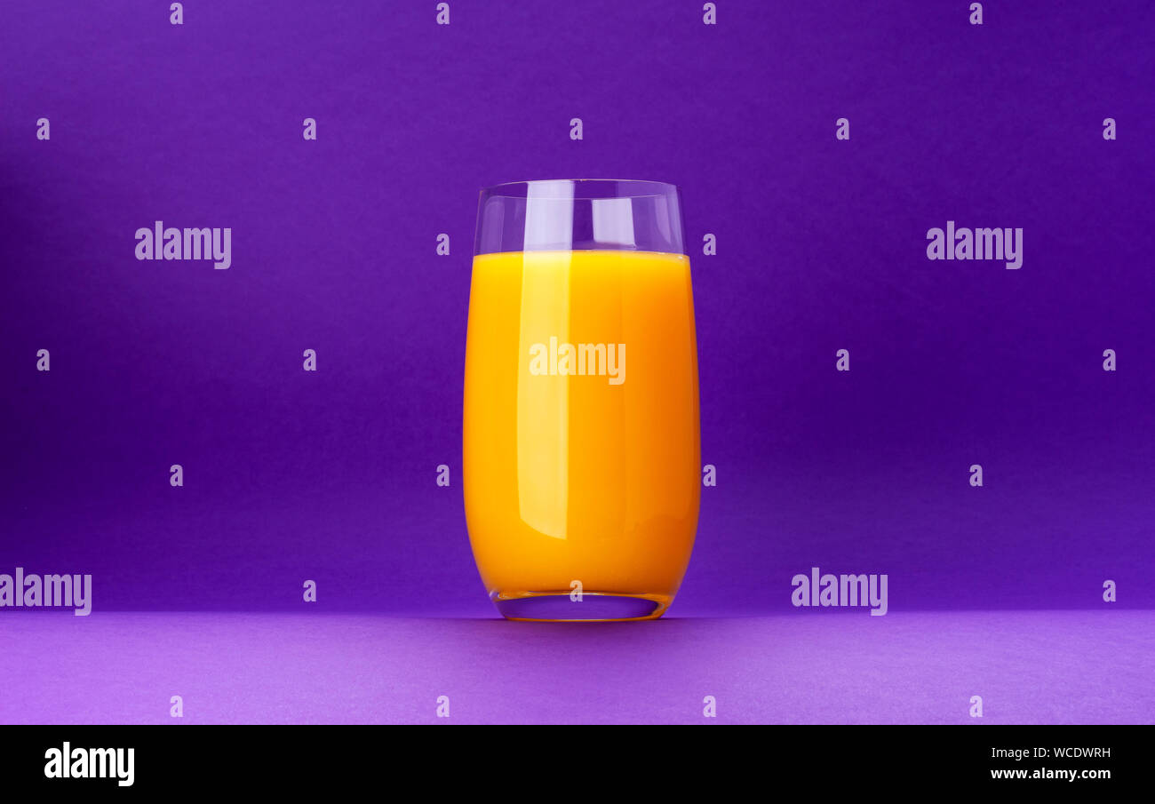 Glass of orange juice isolated on violet background with copy space ...