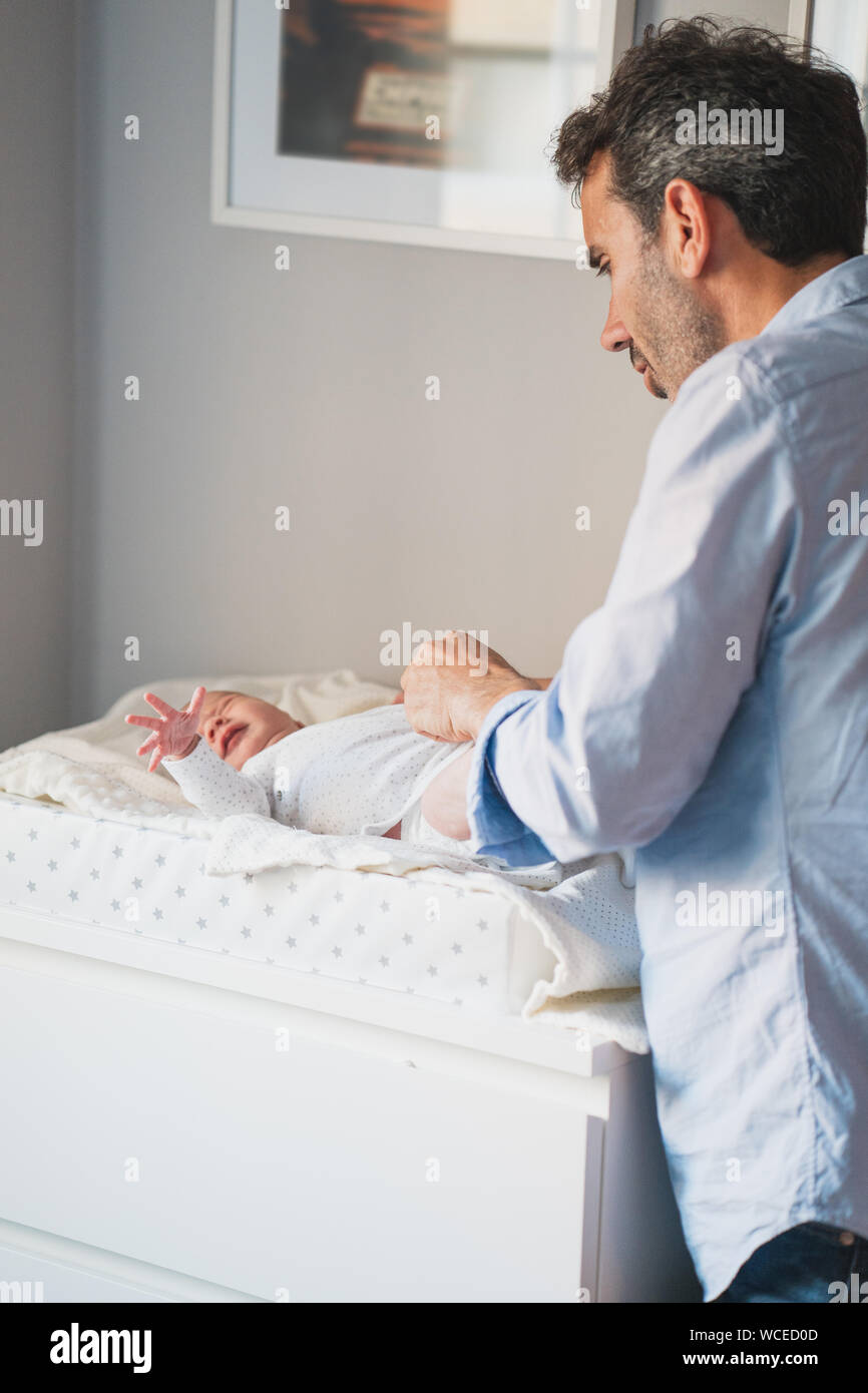 New father changing the diaper to his cute newborn. Baby expresses calm ...
