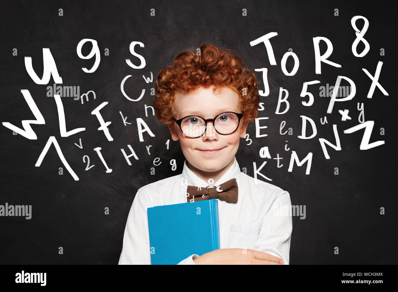 Cute little boy with blue book on chalkboard background Stock Photo - Alamy