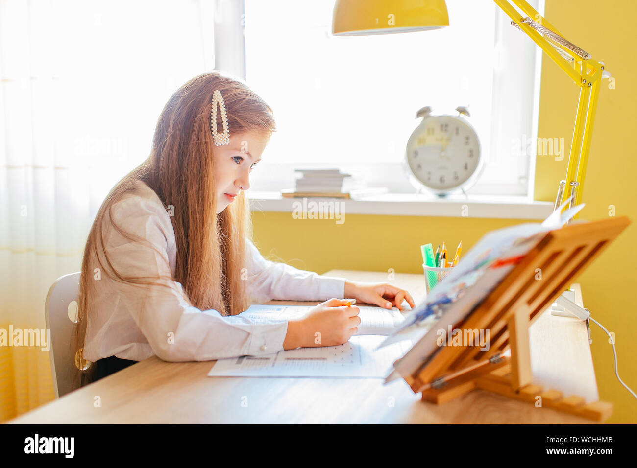 Education at home concept - Cute little girl with long hair studying or completing home work on ...