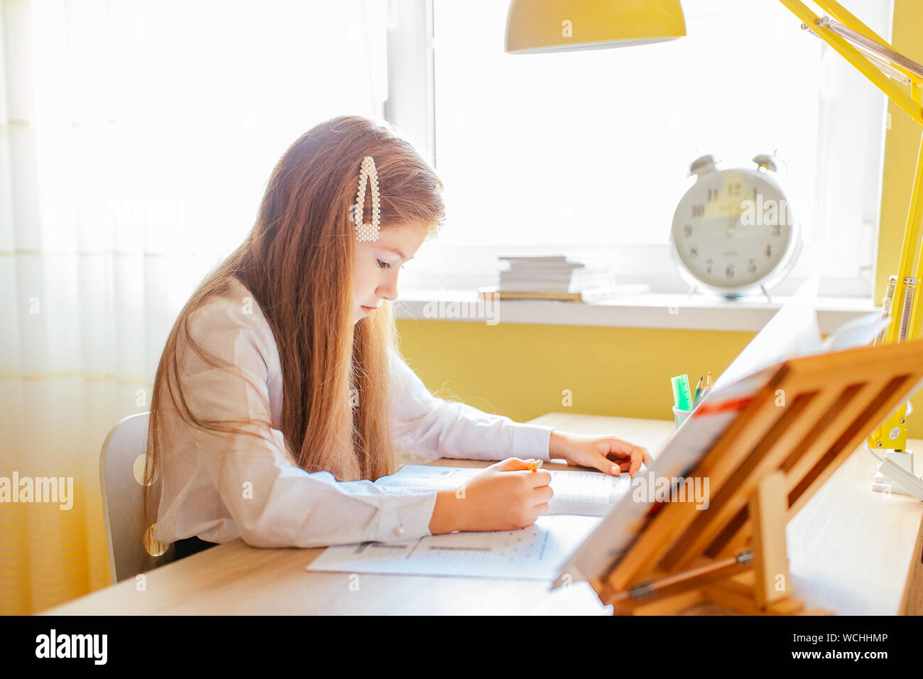 Education at home concept - Cute little girl with long hair studying or completing home work on ...